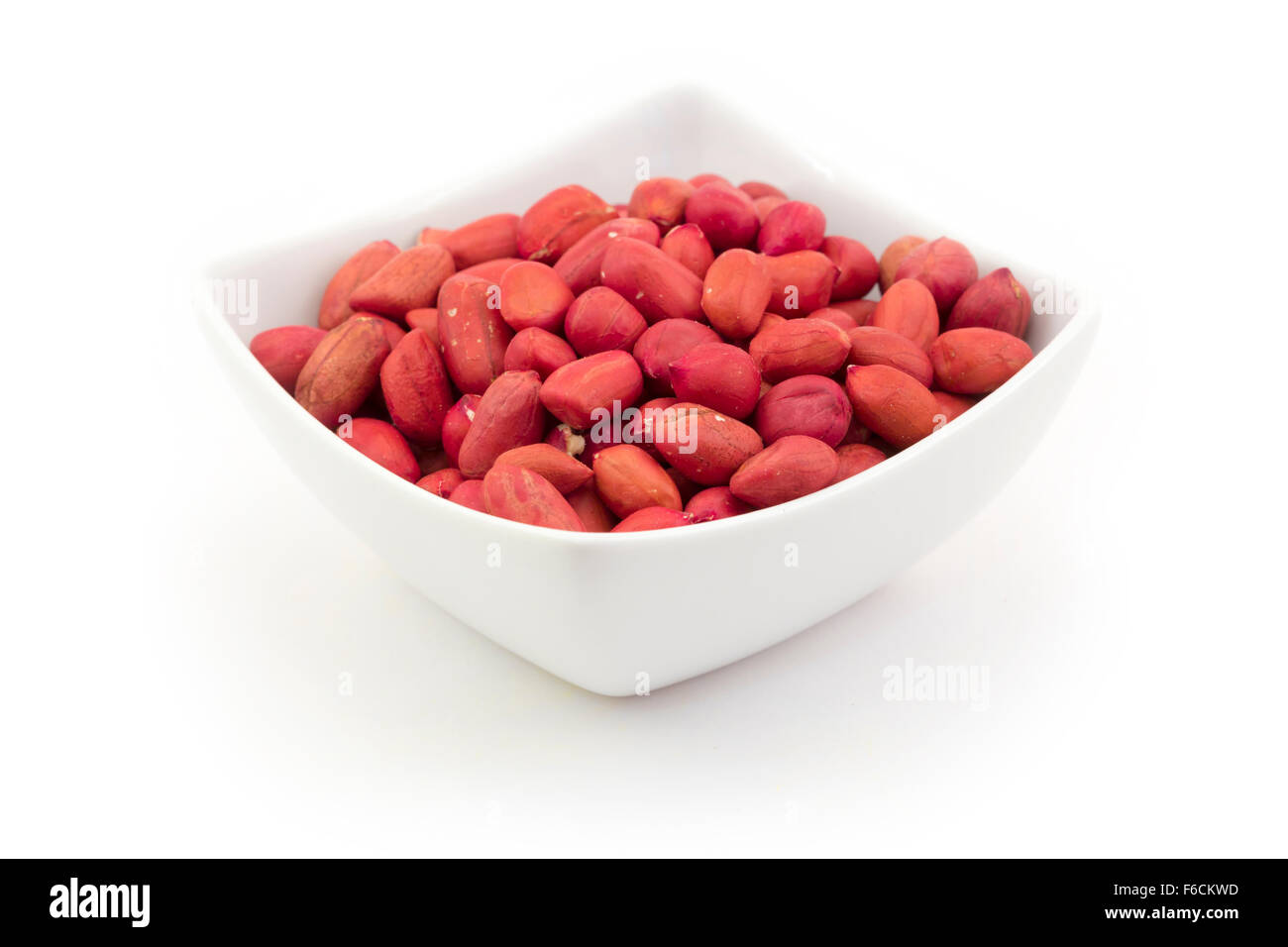 Some whole red-skinned peanuts (groundnuts) in a bowl against a white ...