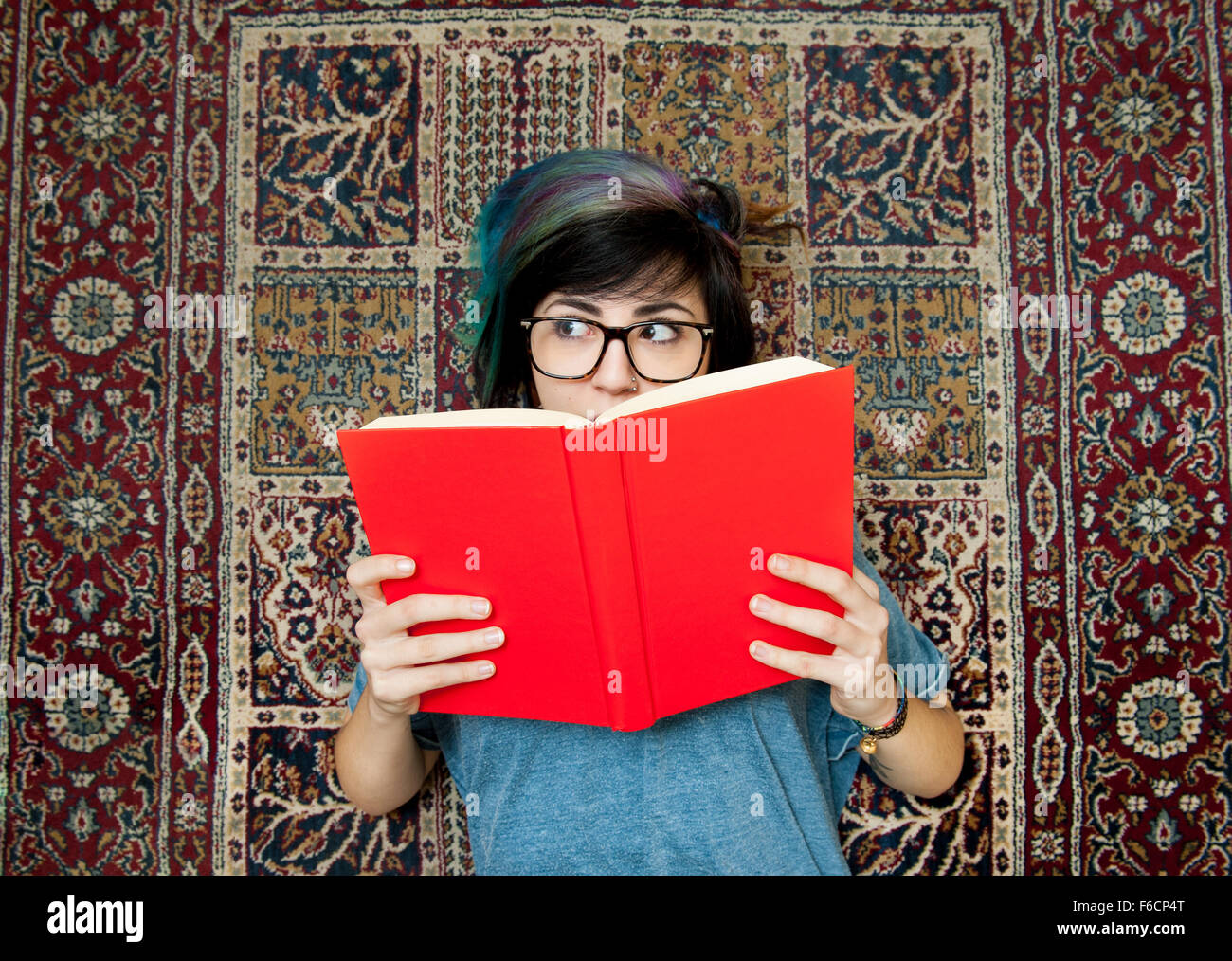 Pretty young woman lying on carpet and reading a red book while looking ...