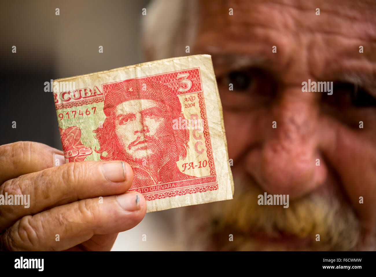 old Cuban man holding a three peso banknote with the portrait of ...