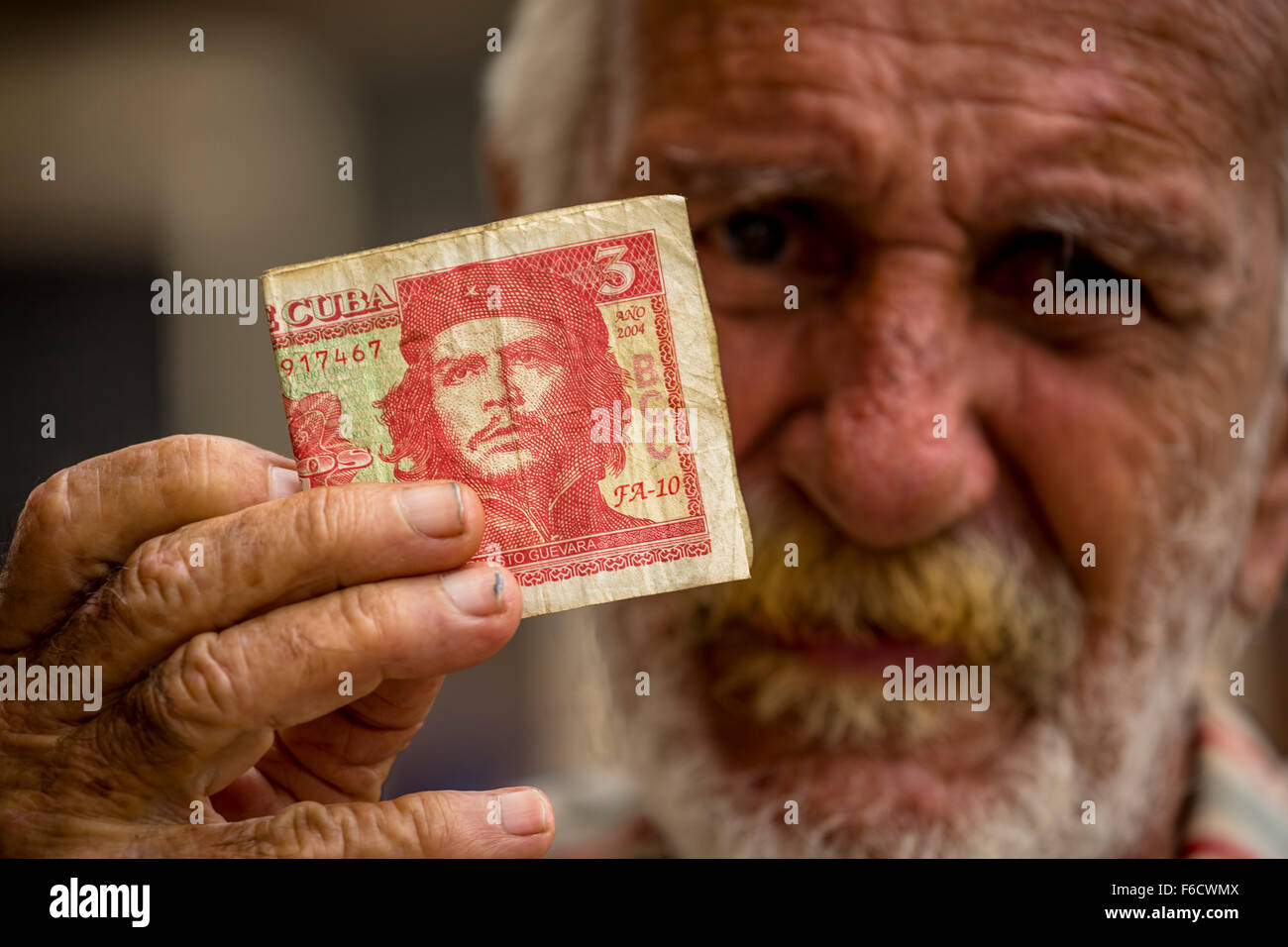 old Cuban man holding a three peso banknote with the portrait of ...