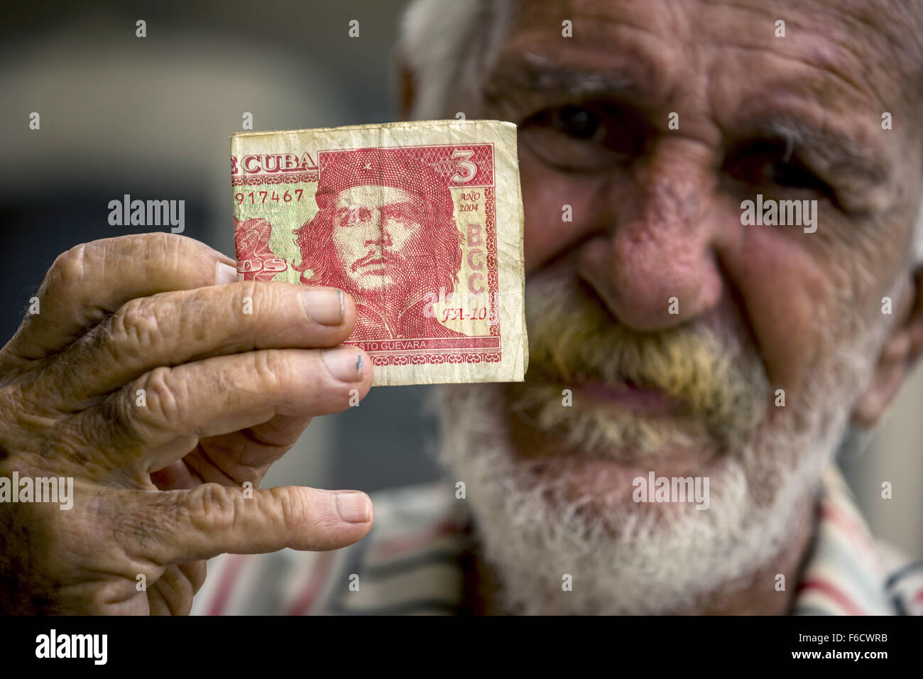 old Cuban man holding a three peso banknote with the portrait of ...