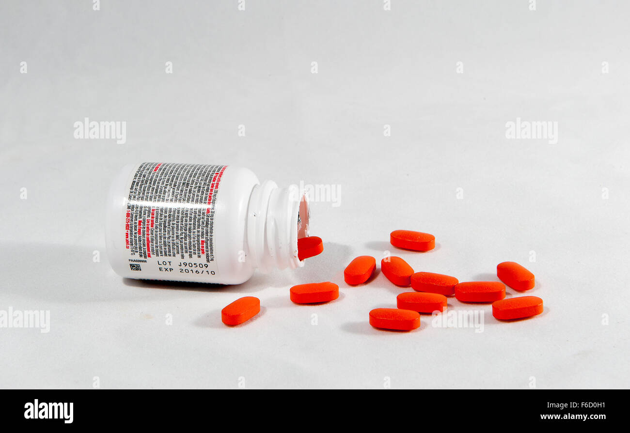 A container of Advil on it's side and spilled tablets against a white ...