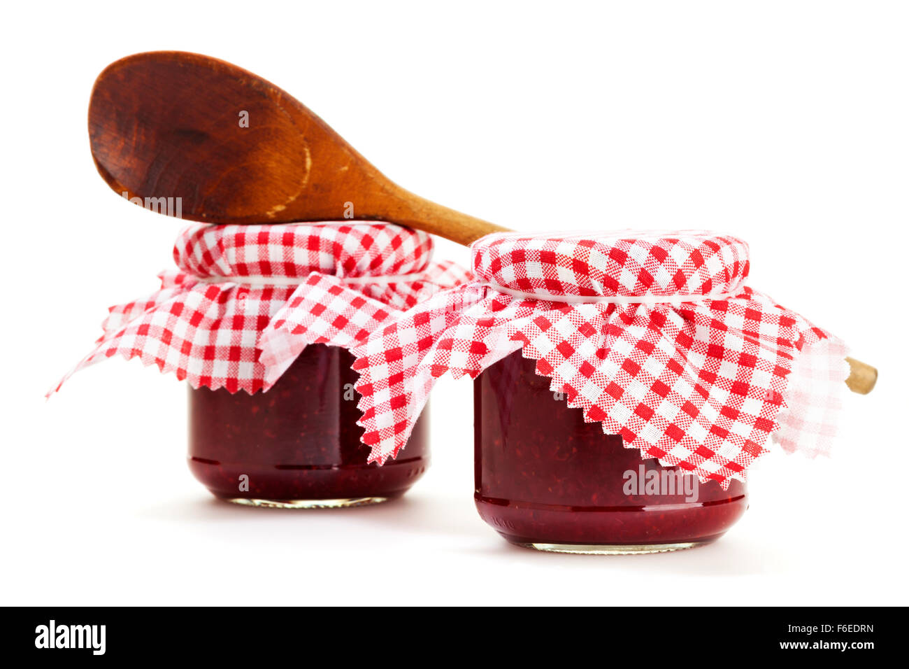 Two jars of homemade jam and wooden cooking spoon isolated on white ...