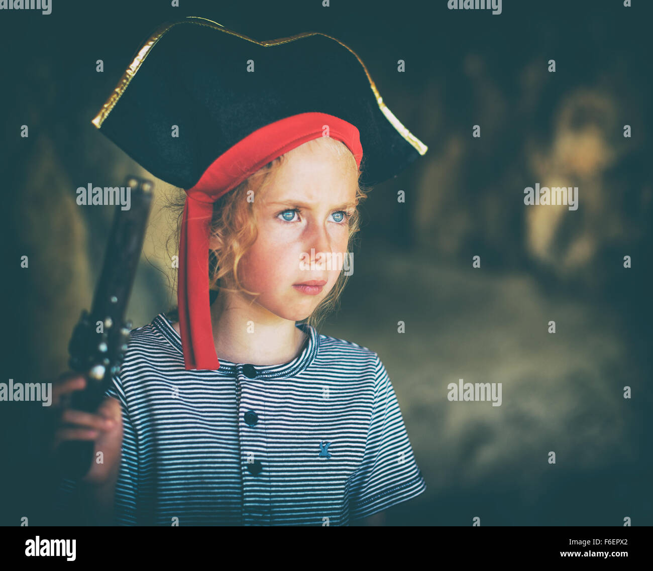 Little girl in pirate costume with musket gun near the cave entrance ...
