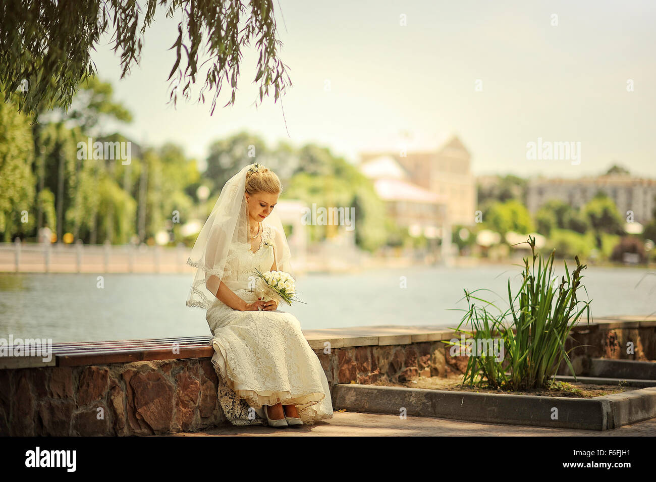 Blonde bride sitting near lake Stock Photo - Alamy