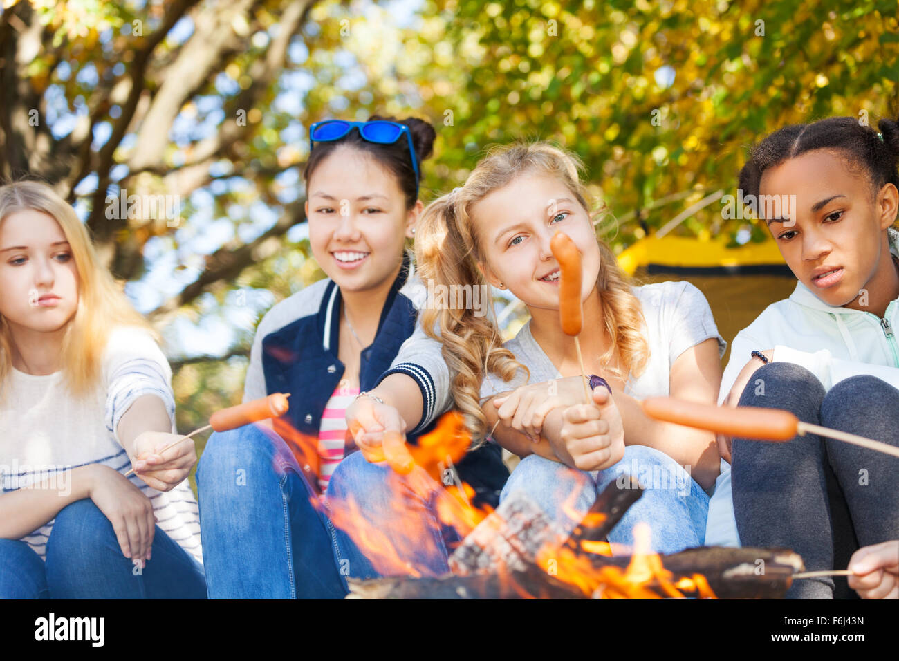 Teen friends sit on campsite with sausages Stock Photo - Alamy