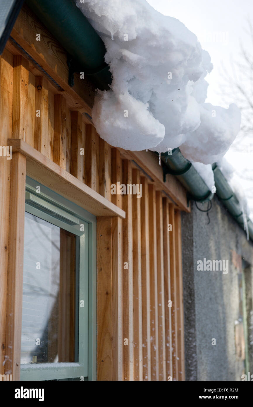 heavy snowfall building up on the guttering of a larch clad building in ...