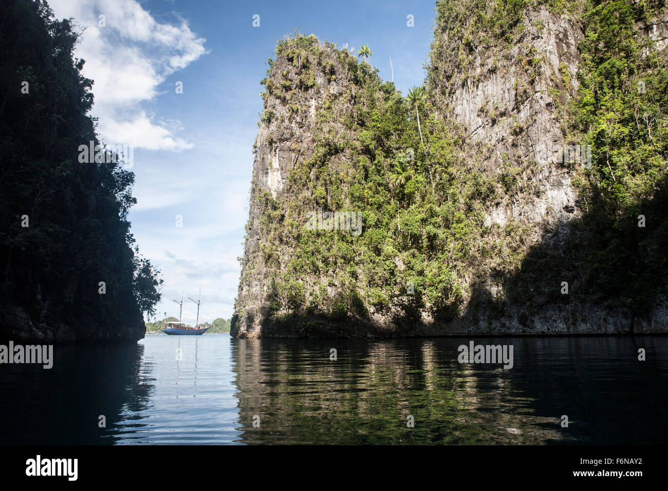 Rugged limestone islands frame an Indonesian pinisi schooner in a ...