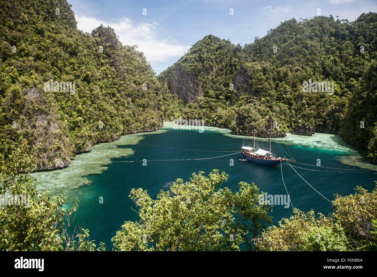 Rugged limestone islands frame an Indonesian pinisi schooner at anchor ...
