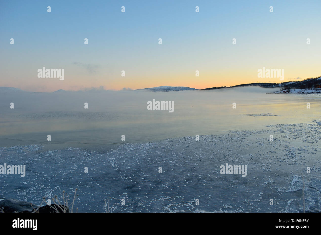 beautiful thick ice fog over cold fjord water with colorful sunset sky ...