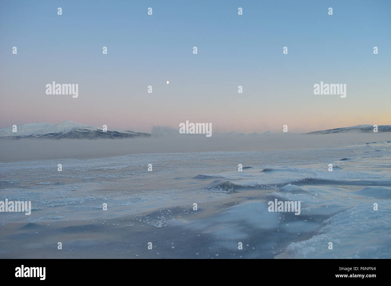 thick sea ice with cold ice frost fog and mist over water with pink ...