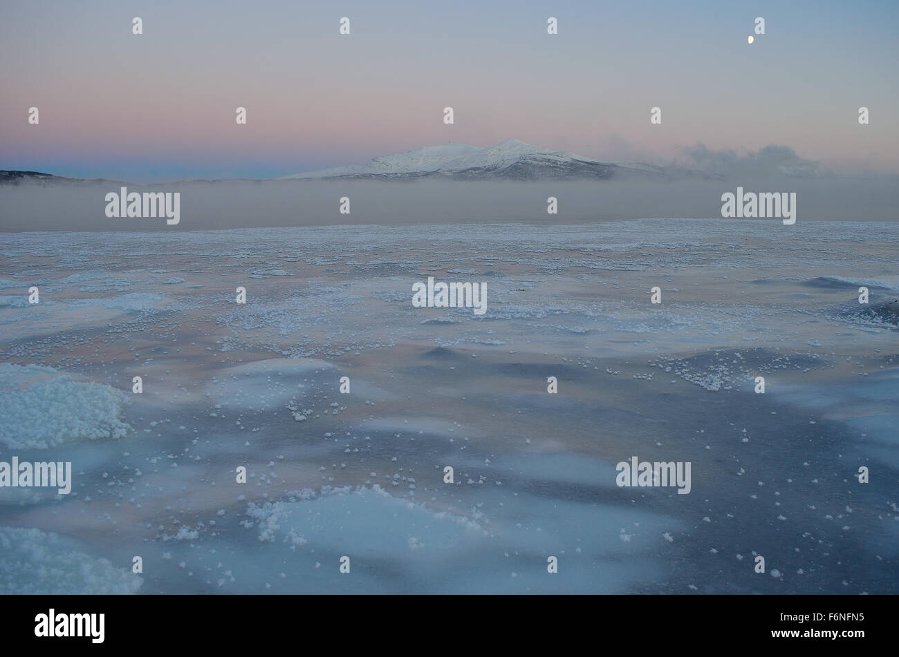 thick sea ice with cold ice frost fog and mist over water with pink ...