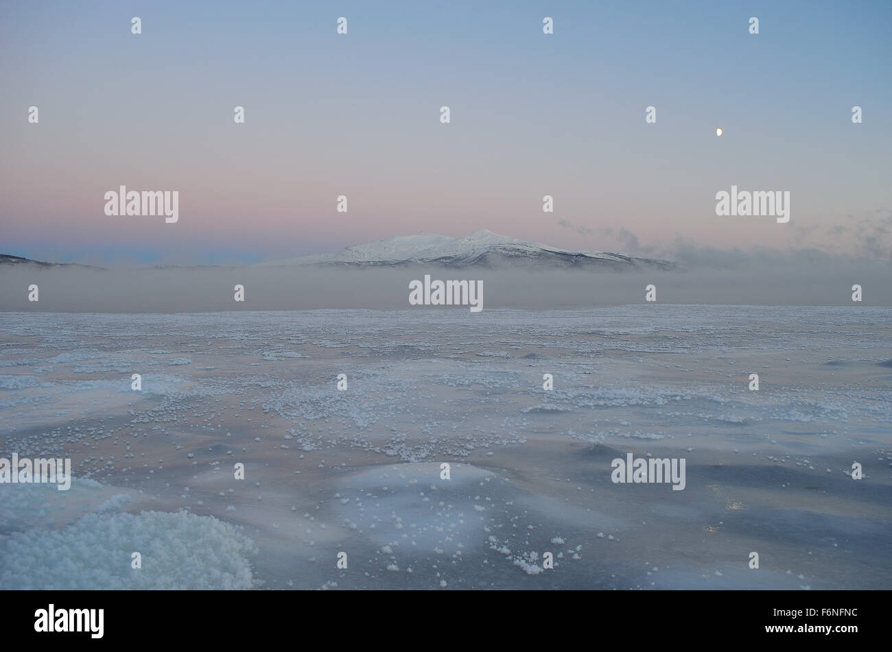 thick sea ice with cold ice frost fog and mist over water with pink ...