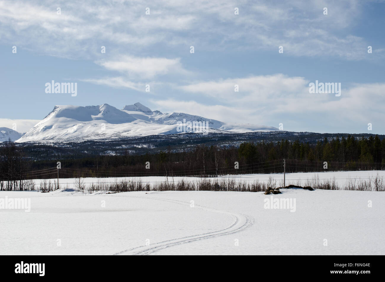white mountain with snowy field on blue sky with long snowmobile track ...