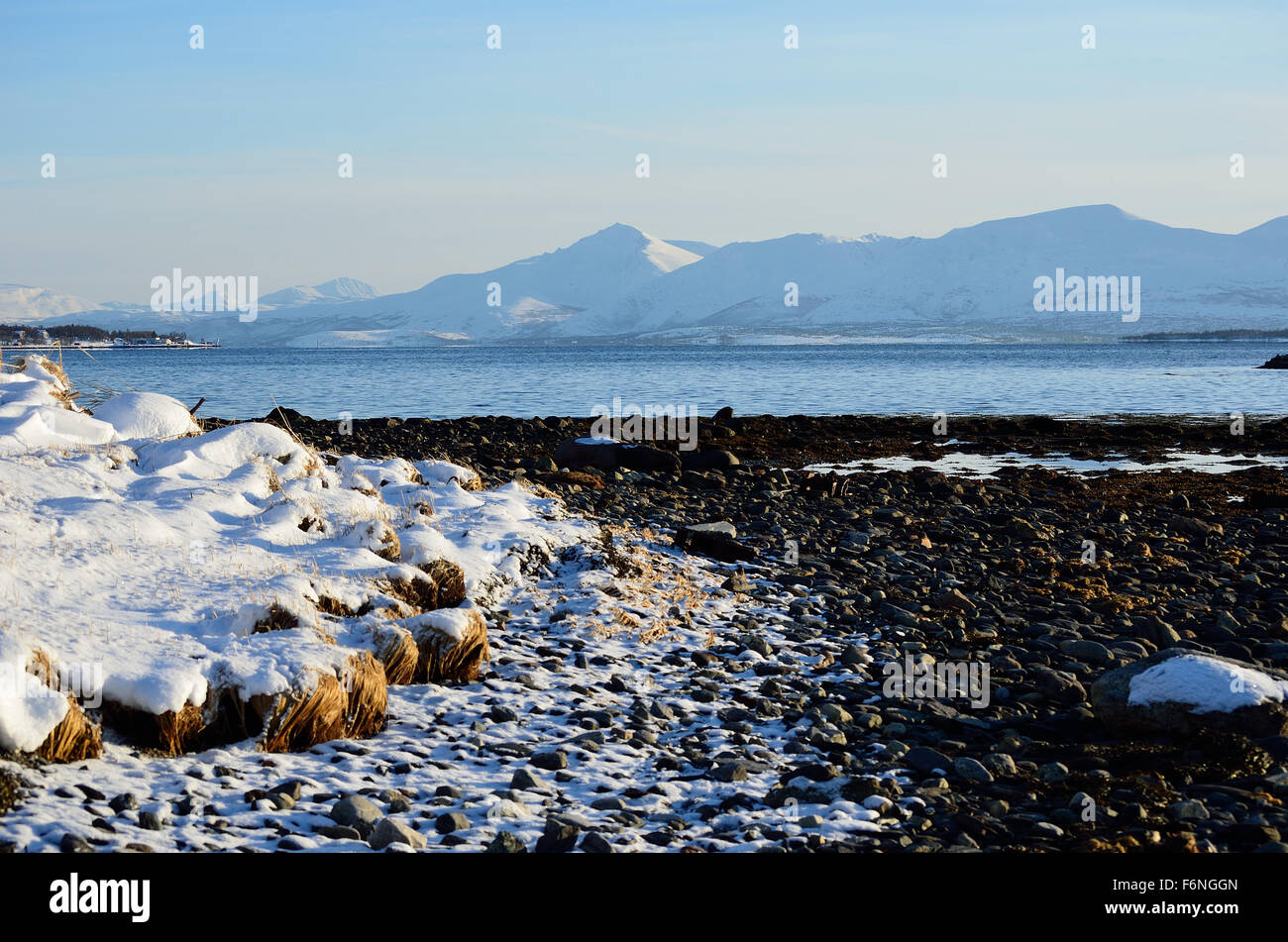 long snowy sea shore in easter sunlight with blue sky, fjord and mighty ...