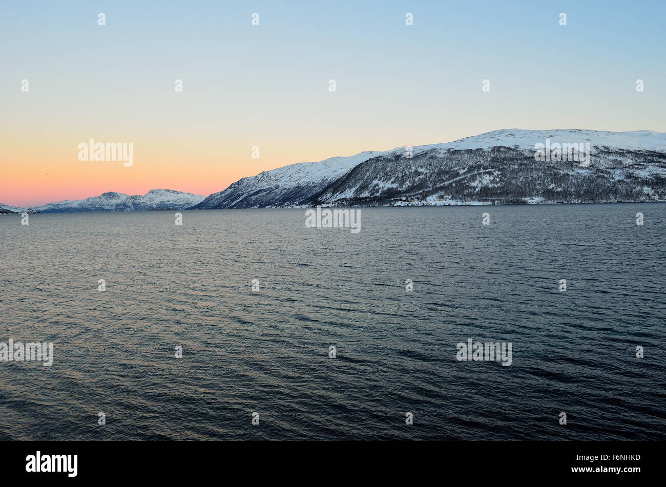 Cold fjord water surrounded by snowy mountains and vibrant dawn sky in ...