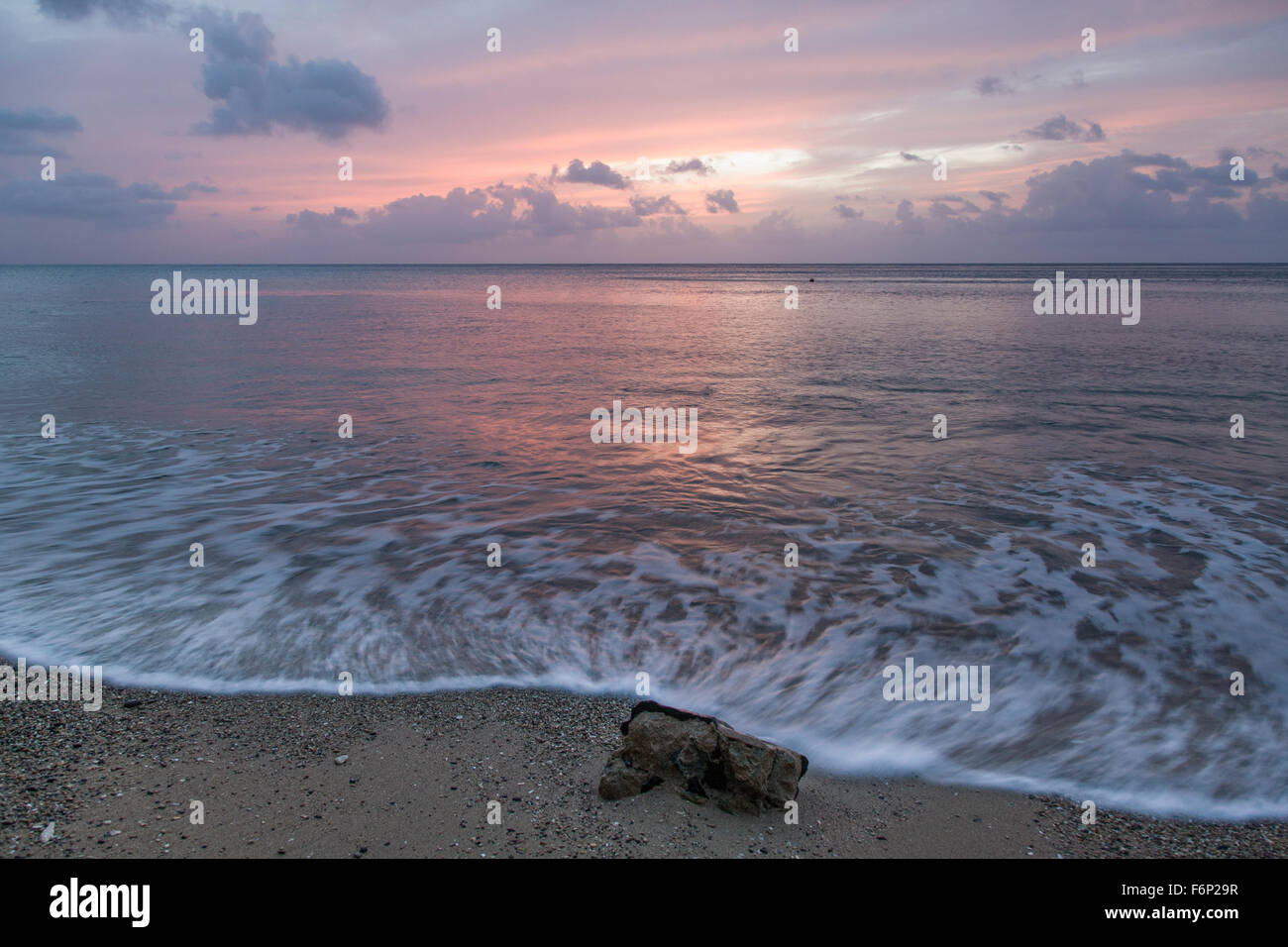 Waves gently swirl over a sandy setting sun colours the tropical sea ...