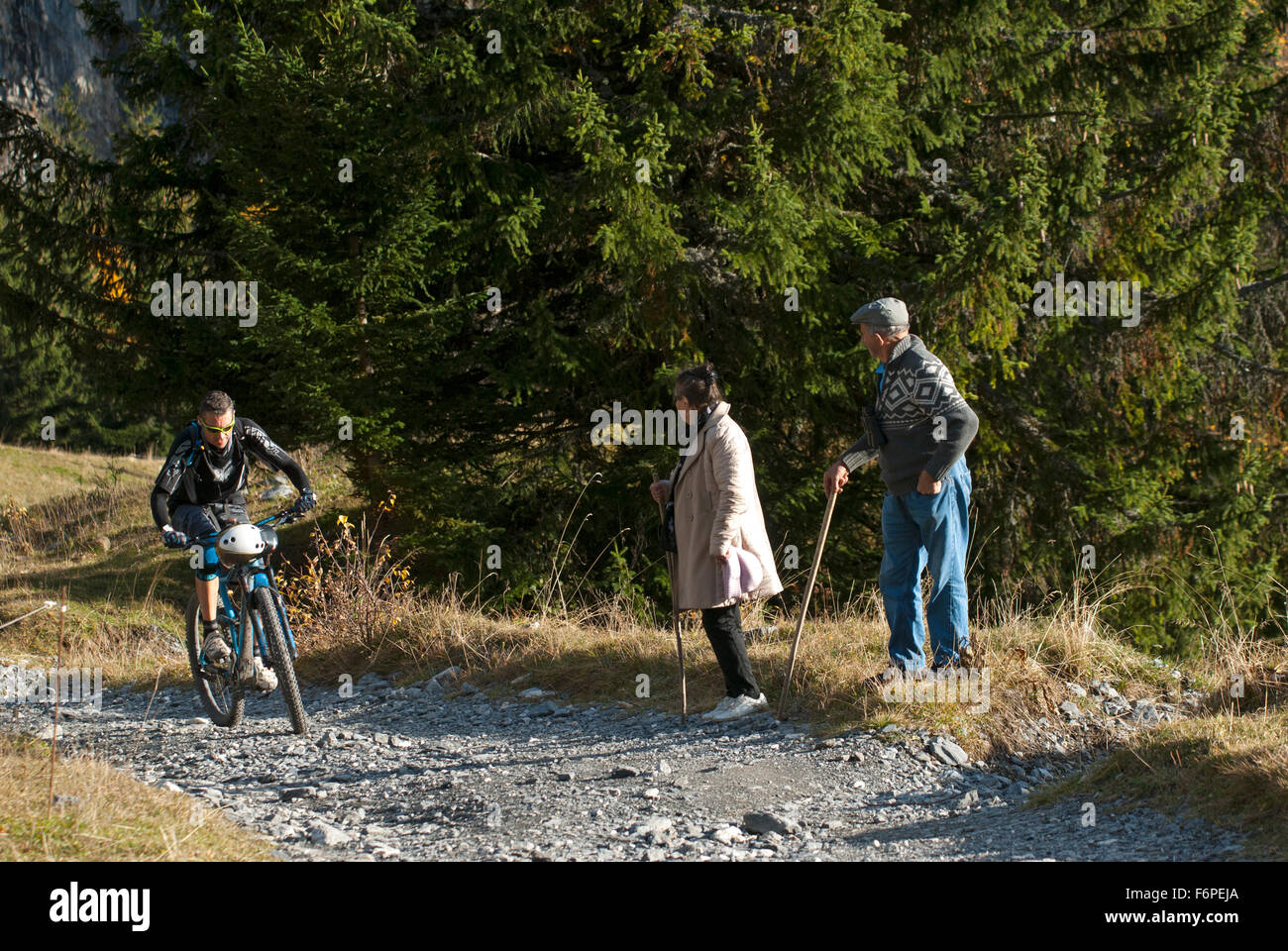 Elderly couple out walking on mountain trail, watching man on mountain ...