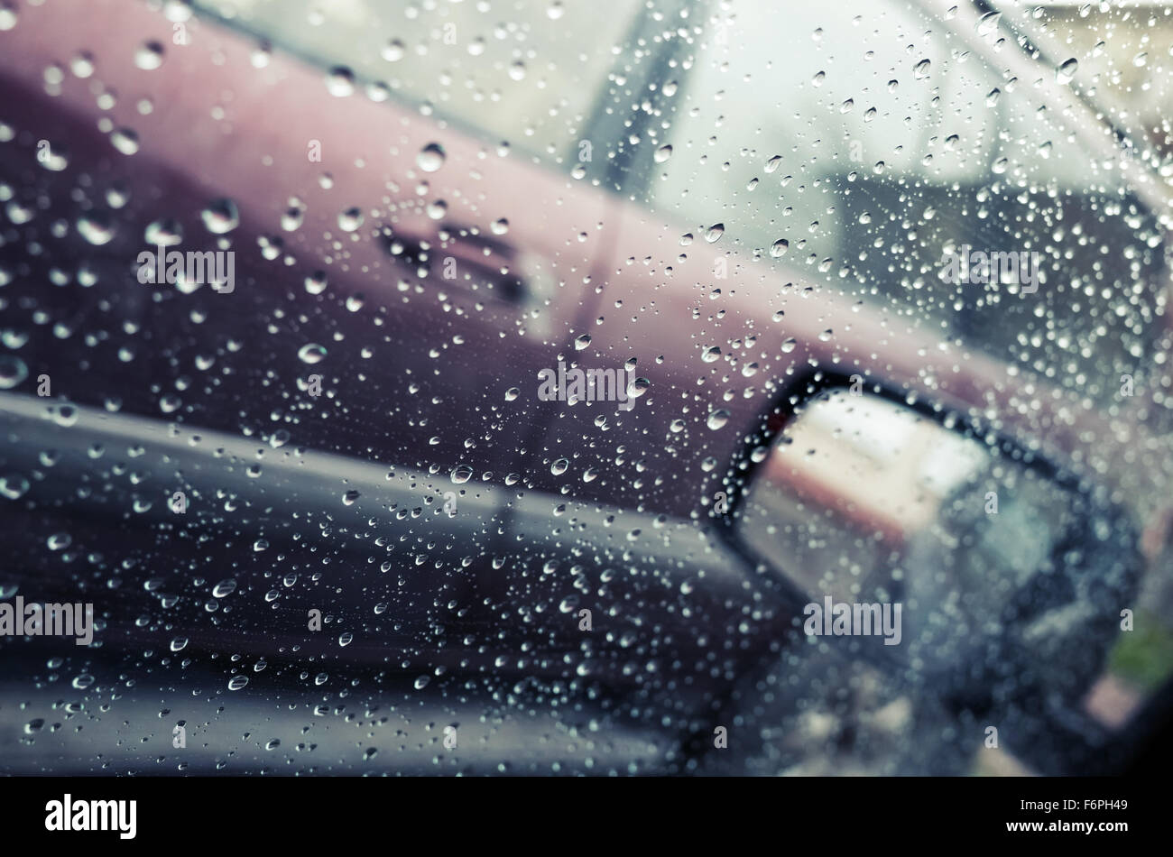Wet car window with raindrops and a mirror behind. Close-up photo with ...
