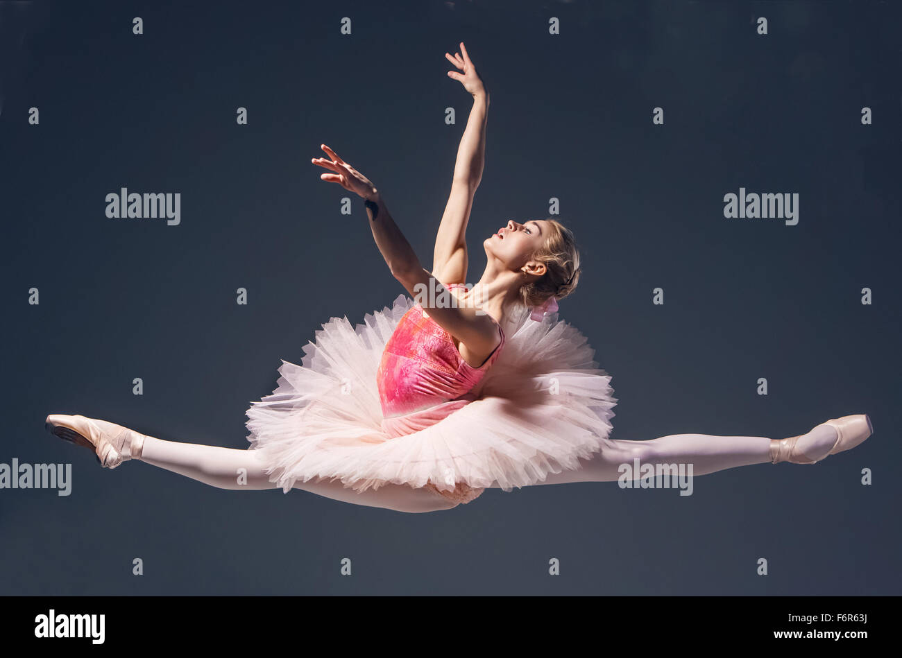 Beautiful female ballet dancer jumping on a gray background. Ballerina is wearing in pink tutu ...