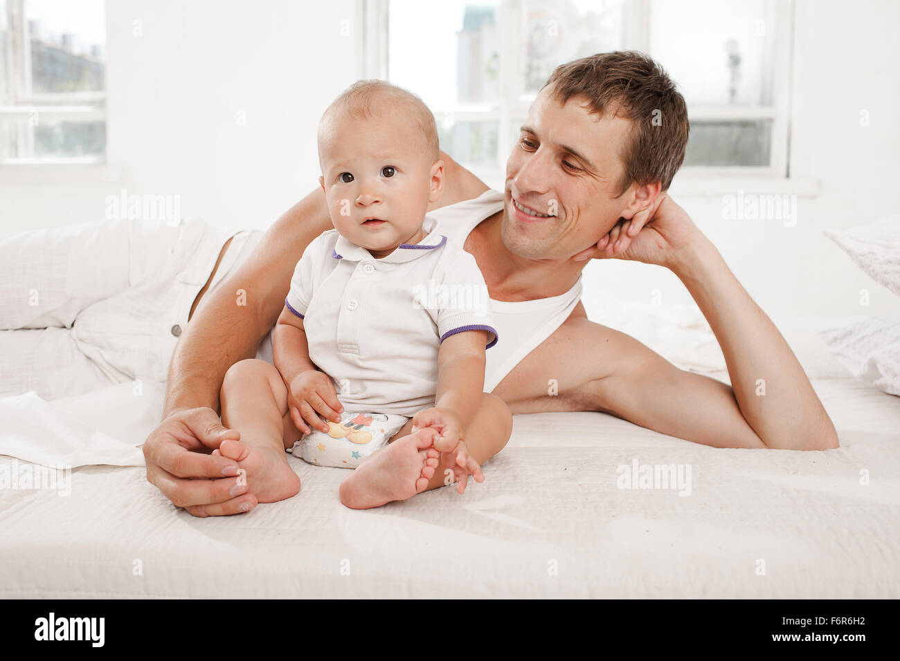 young father with his nine months old son on the bed at home on white ...