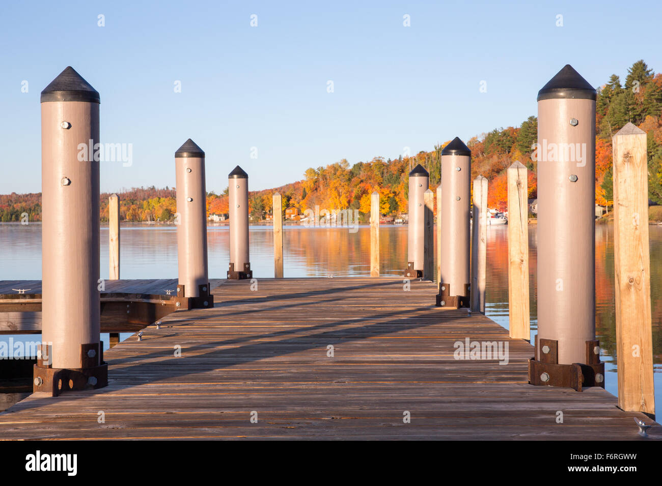 Pier leading to a smooth lake, colorful shoreline, and clear sky with ...