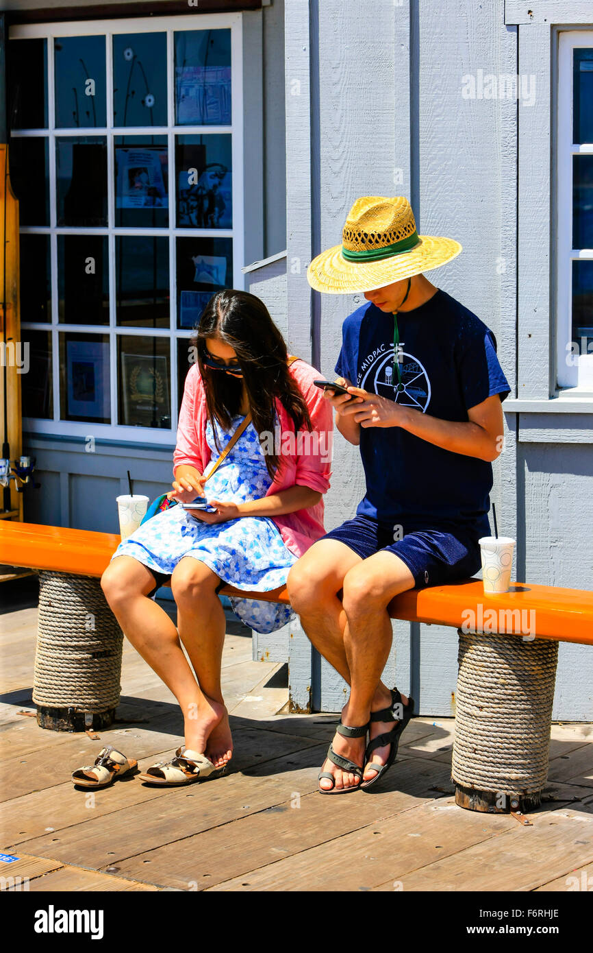 Two people sitting on a bench seat interacting with their cellphones ...