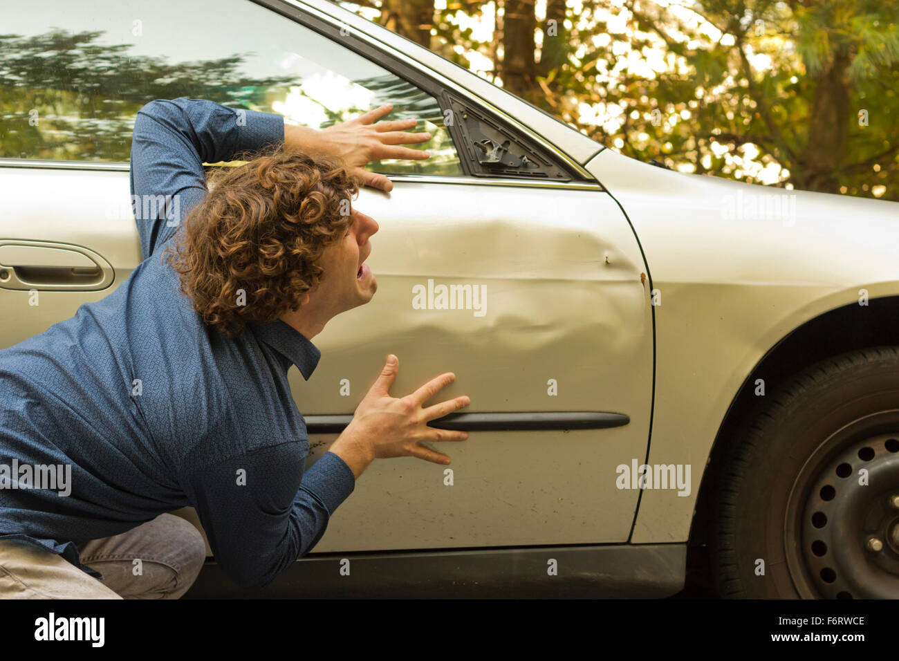 Silly man makes angry annoyed facial expression about dame to his car ...