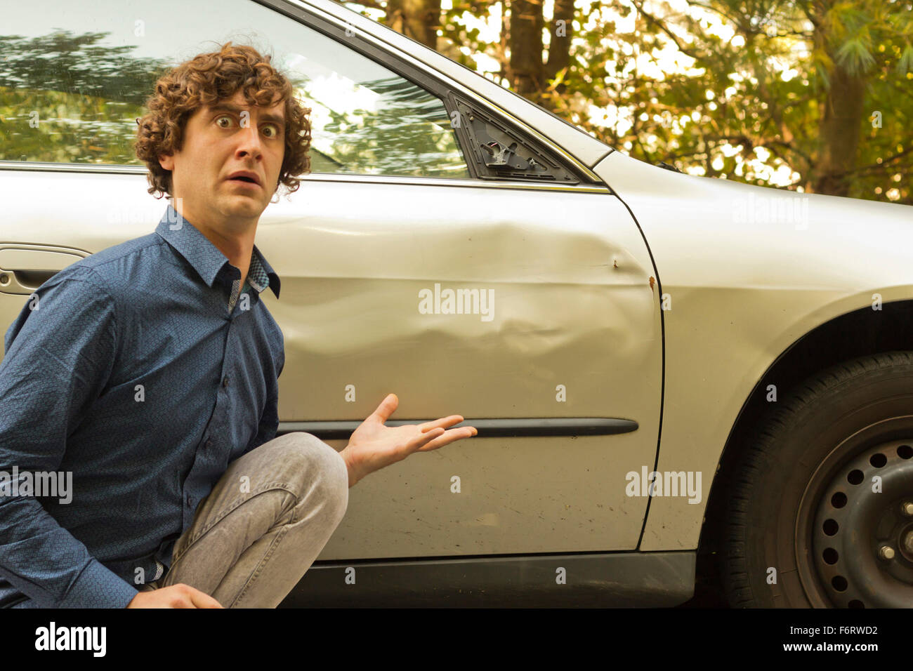 Silly man makes angry annoyed facial expression about dame to his car ...