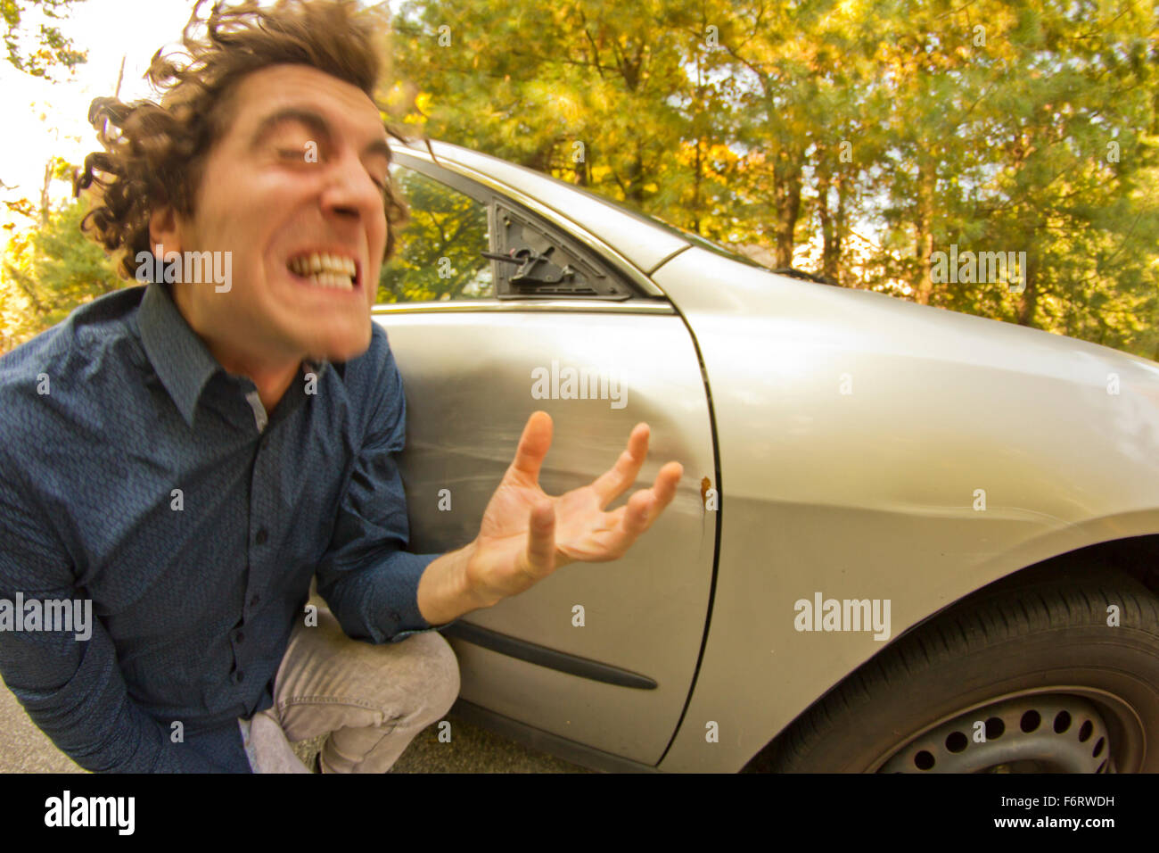 Silly man makes angry annoyed facial expression about dame to his car ...