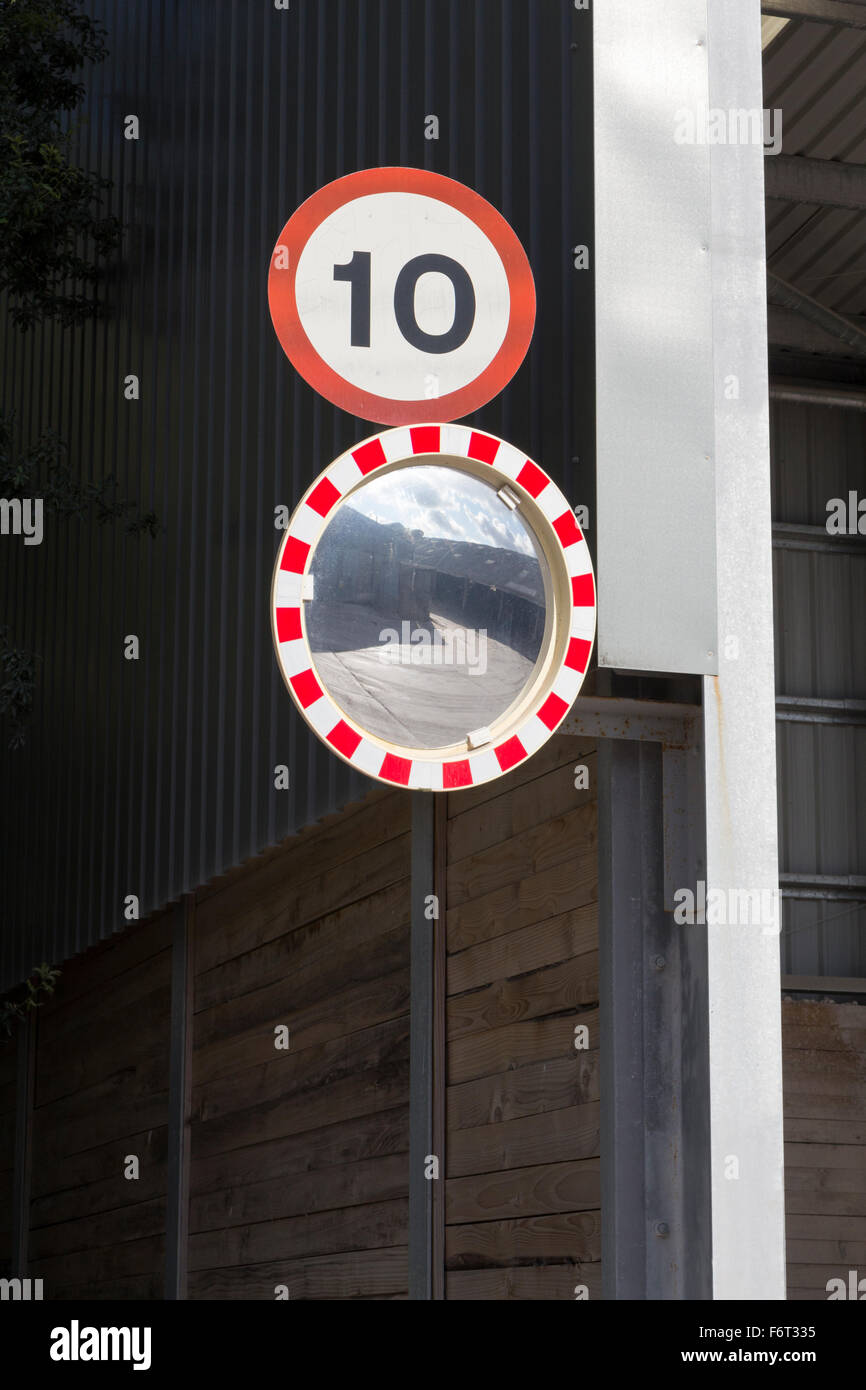 A convex road safety mirror and speed limit sign on an industrial site ...