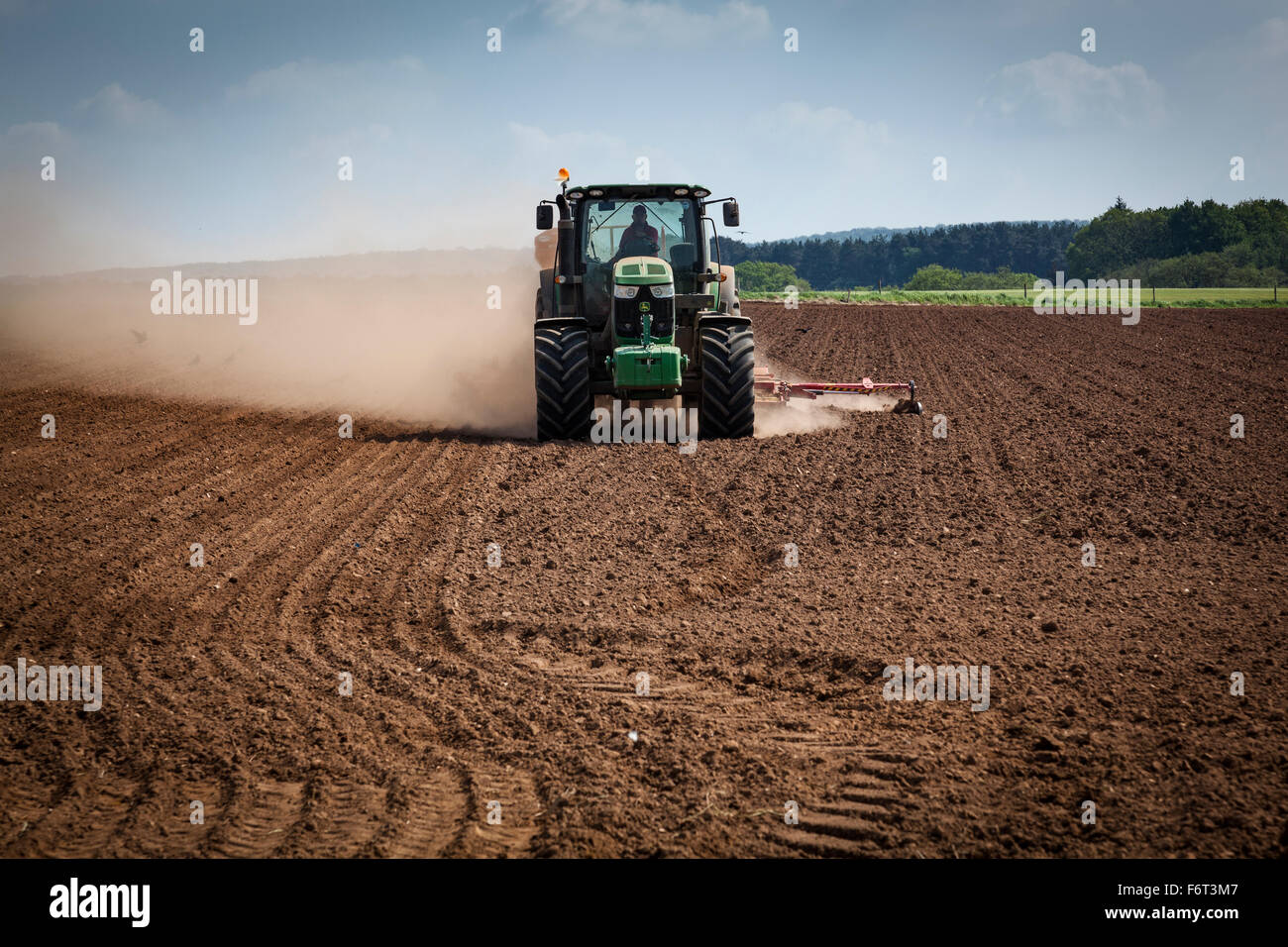 Tractor creates dust as it tows a large seed drill behind it whilst ...