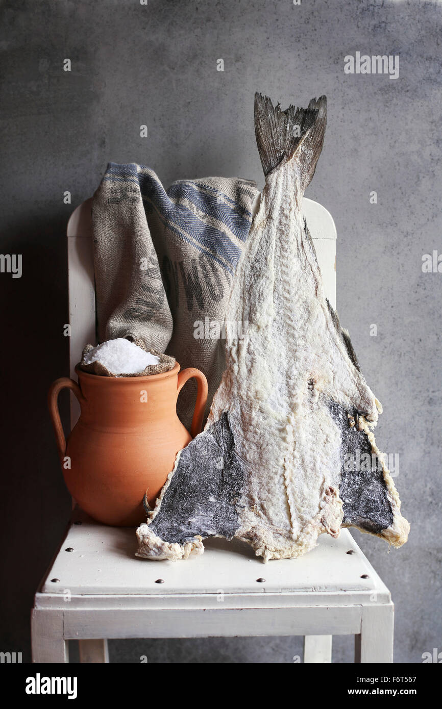 Salted cod fish and a rustic clay pot with sea salt on a white chair ...