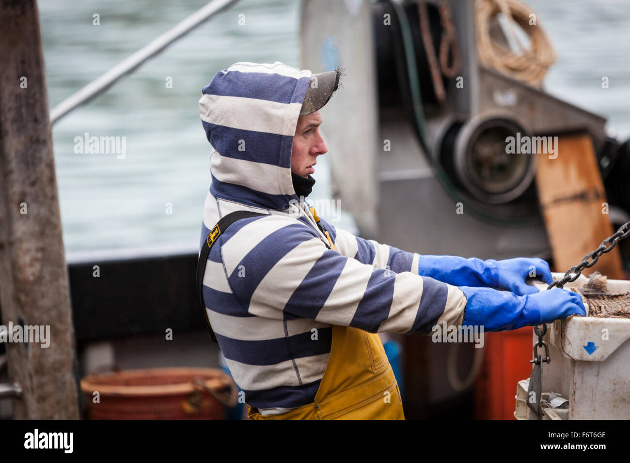 A fisherman wearing yellow oilskins and a blue and white striped hoodie ...