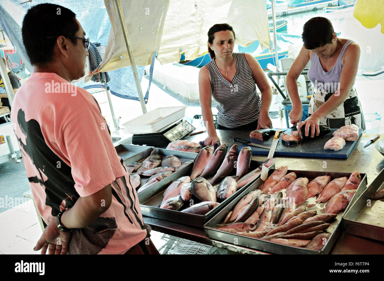 Women cutting fish for a customer at the fish market of Marsaxlokk ...