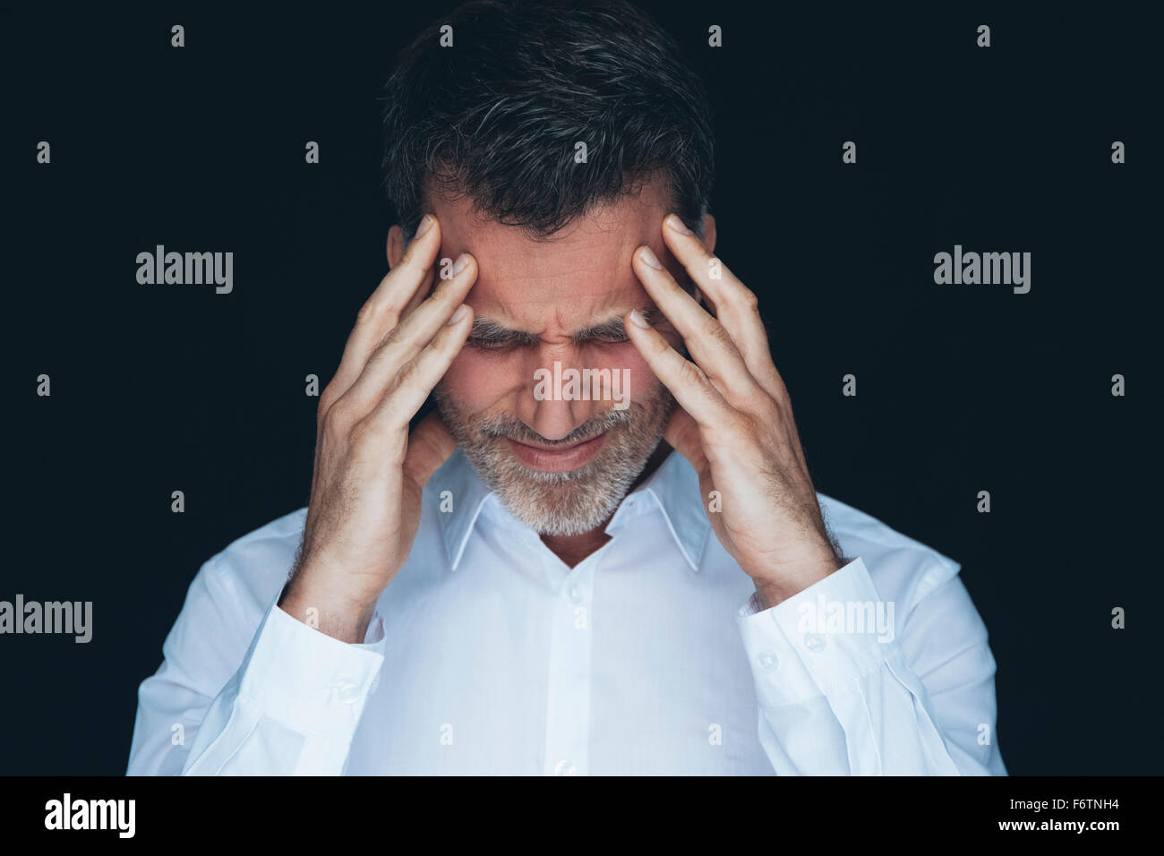 Portrait of man with hands on his forehead in front of black background ...