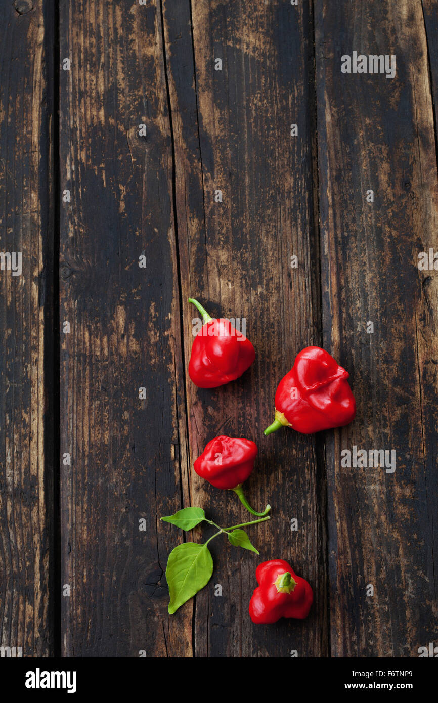 Four red chili bell peppers on dark wood Stock Photo - Alamy