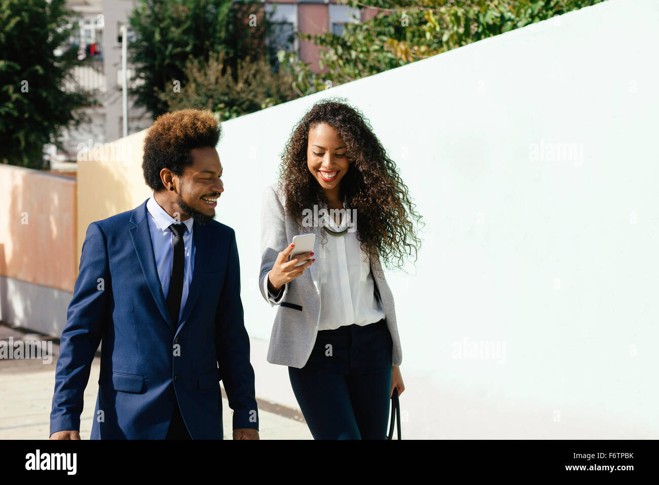 Portrait of two smiling young business people looking at smartphone ...