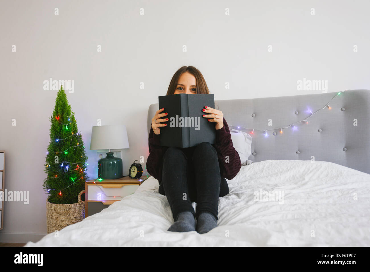 Woman sitting on bed hiding behind a book Stock Photo - Alamy