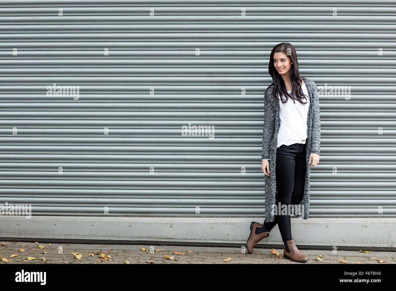 Smiling young woman standing in front of roller shutter Stock Photo - Alamy