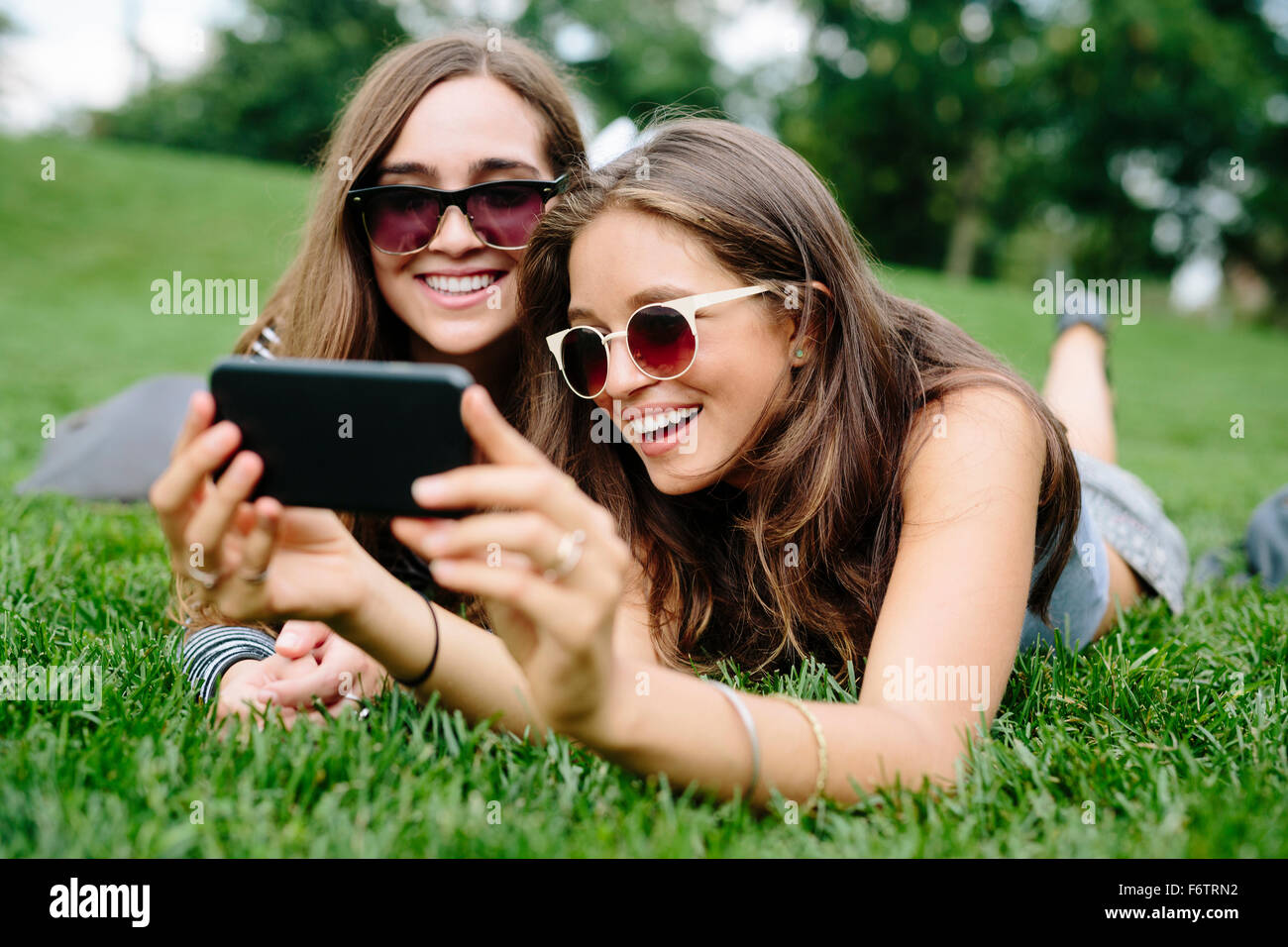 Two happy friends in a park looking at cell phone Stock Photo - Alamy