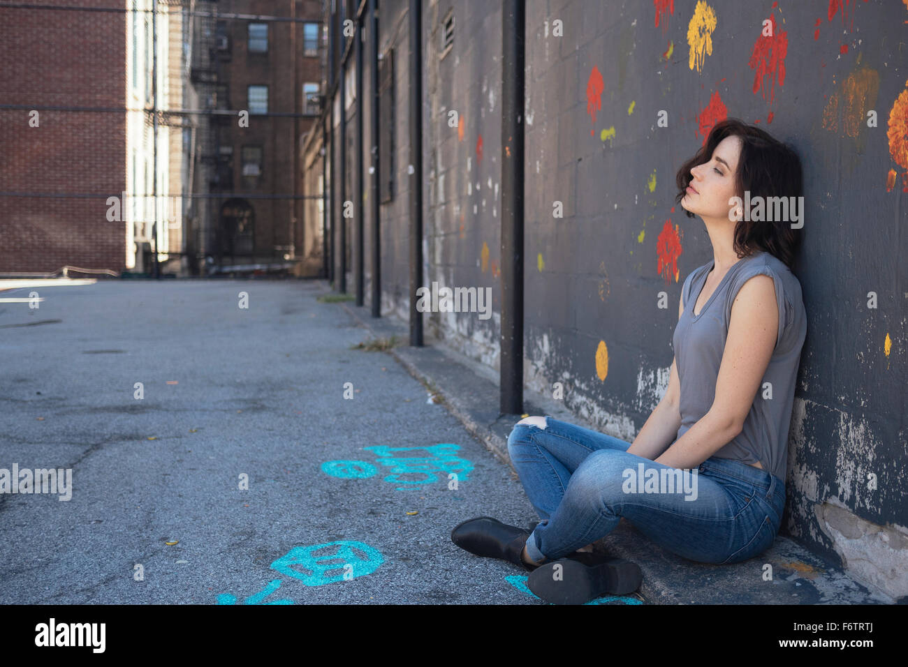 USA, New York City, young woman sitting on the ground leaning against a ...