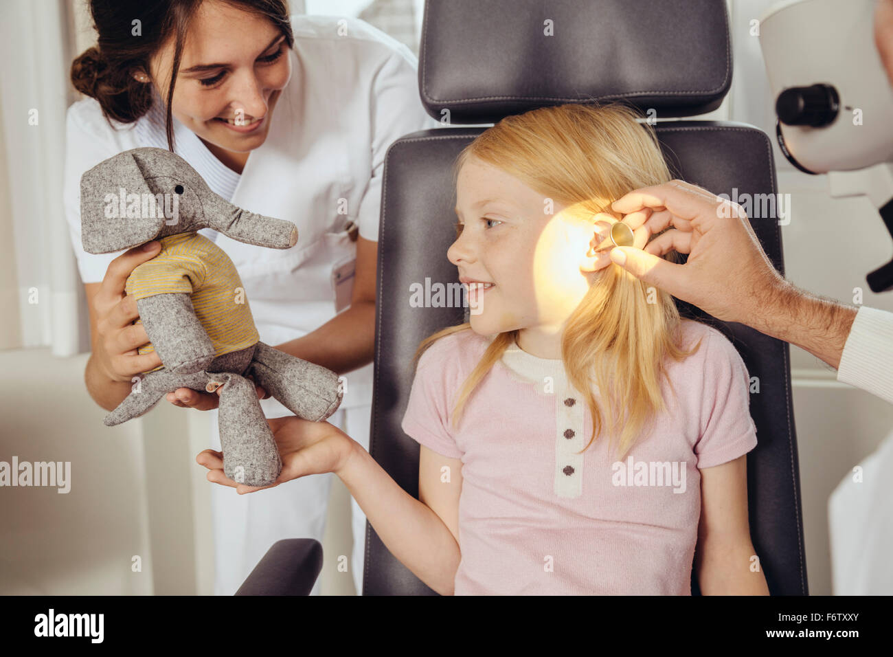 Nurse distracting child with toy while doctor using surgical microscope ...