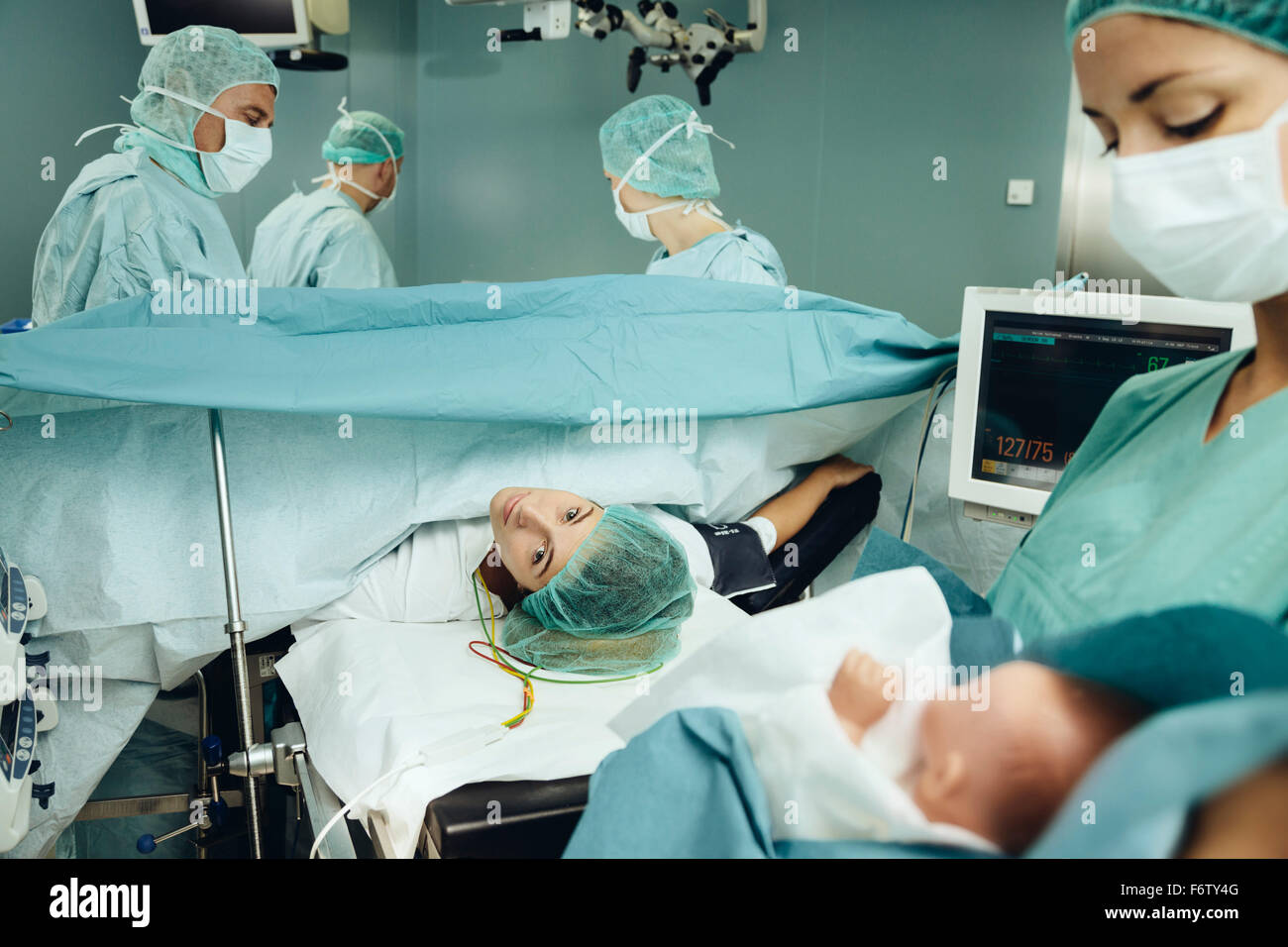 Operating room nurse bringing baby to mother while team finishing c ...