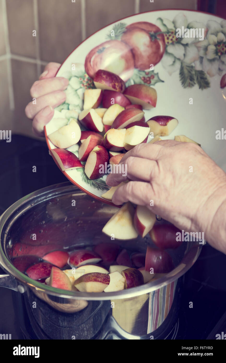 Senior woman putting pieces of apples in a cooking pot for preparing ...