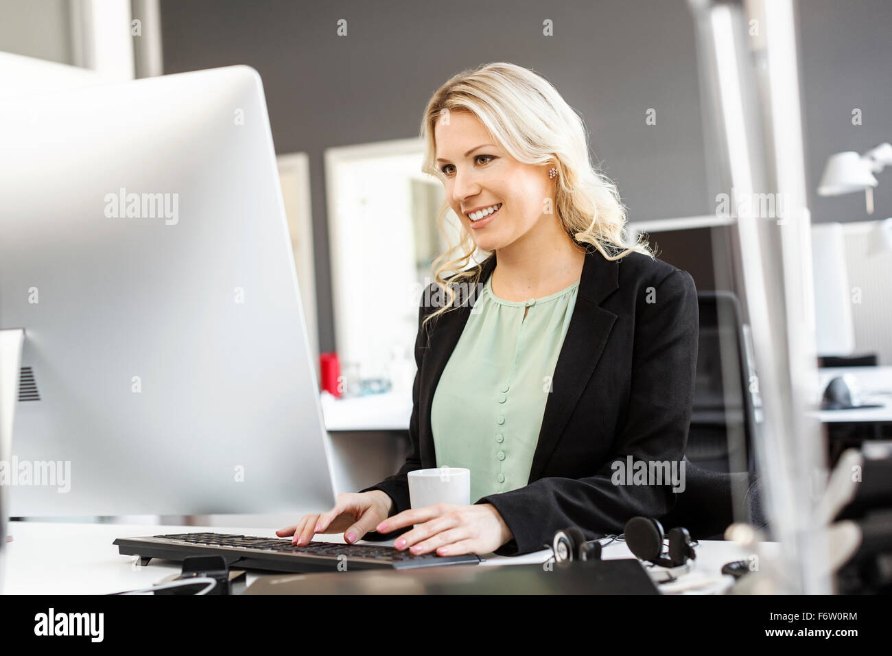 Smiling blond woman working at desk in office Stock Photo - Alamy