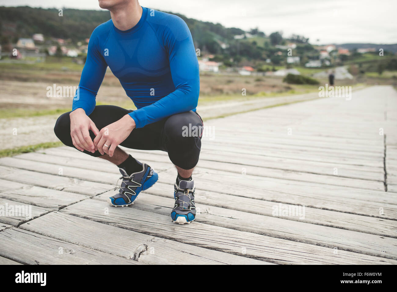 Runner squatting on wooden path Stock Photo - Alamy