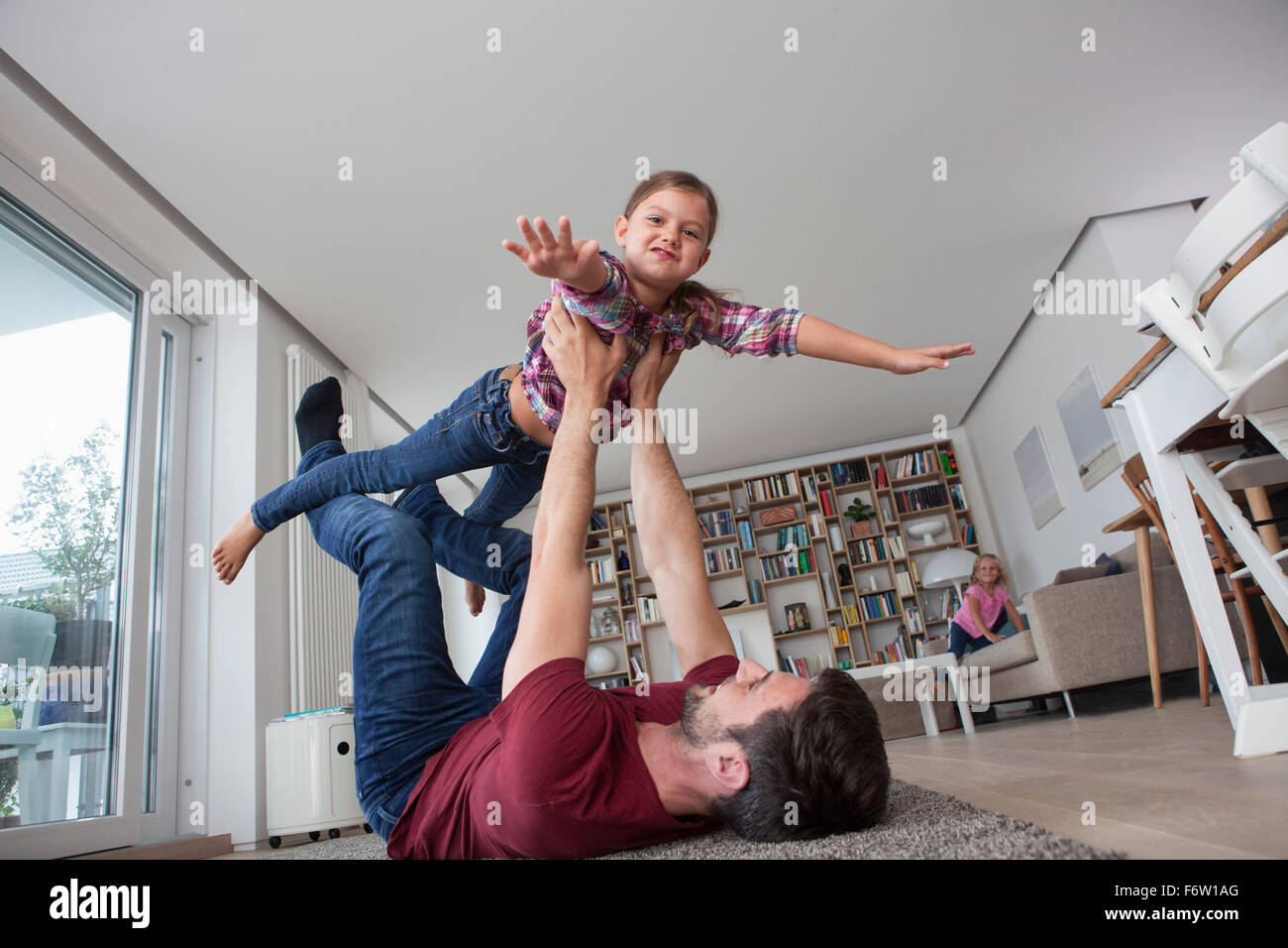Man lying on the floor at living room playing with his little daughter ...