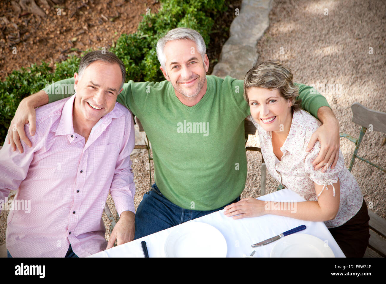 Portrait of three smiling friends sitting in the garden looking up to ...