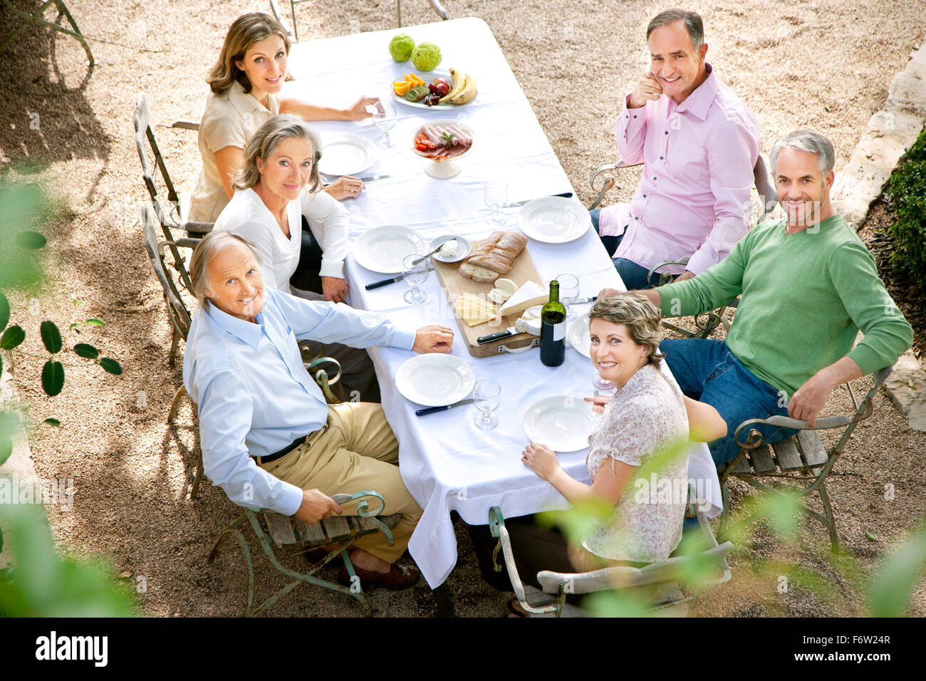 Six friends sitting at laid table in the garden looking up to camera ...